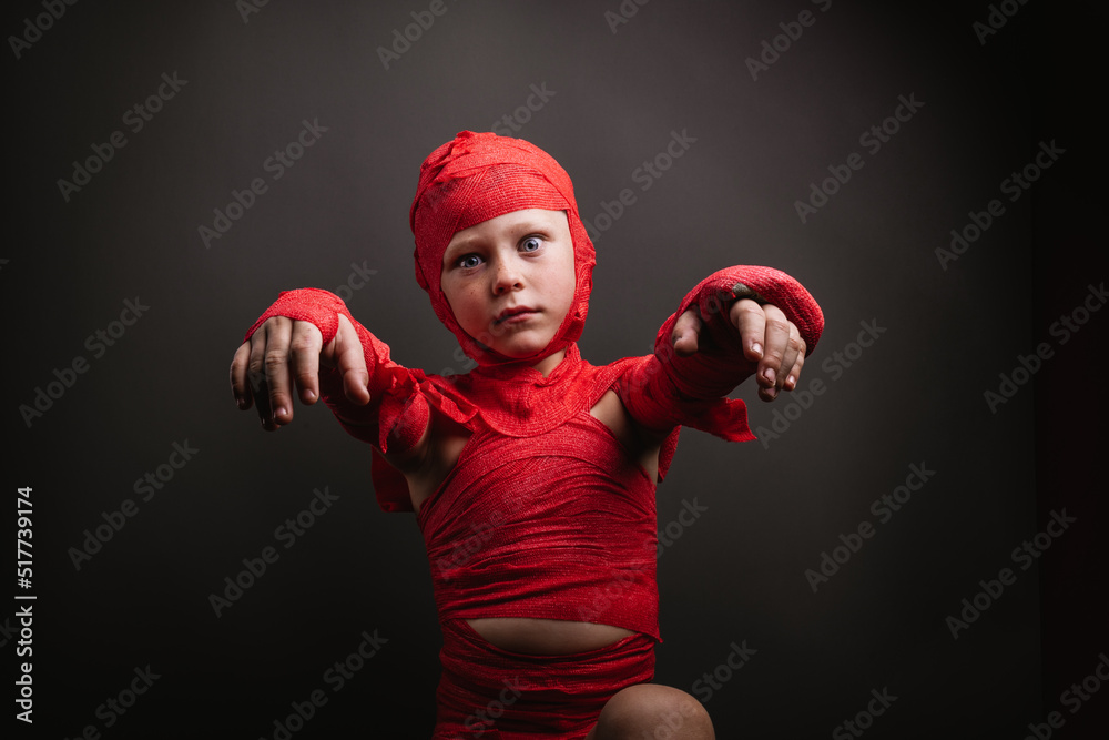 Cute little kid in mummy costume shouting and gesturing in grey studio ...