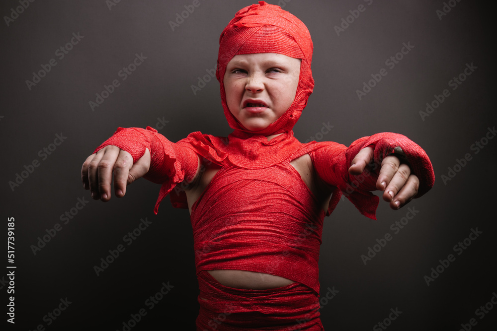 Cute little kid in mummy costume shouting and gesturing in grey studio ...
