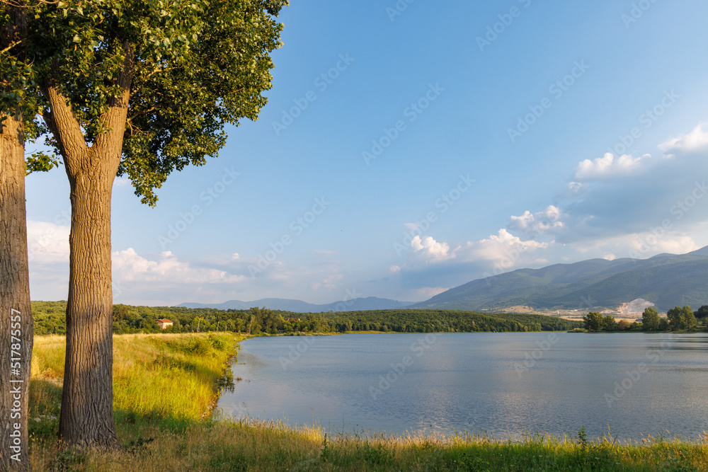 Deciduous trees grow on ledge above lake against backdrop of mountain ...