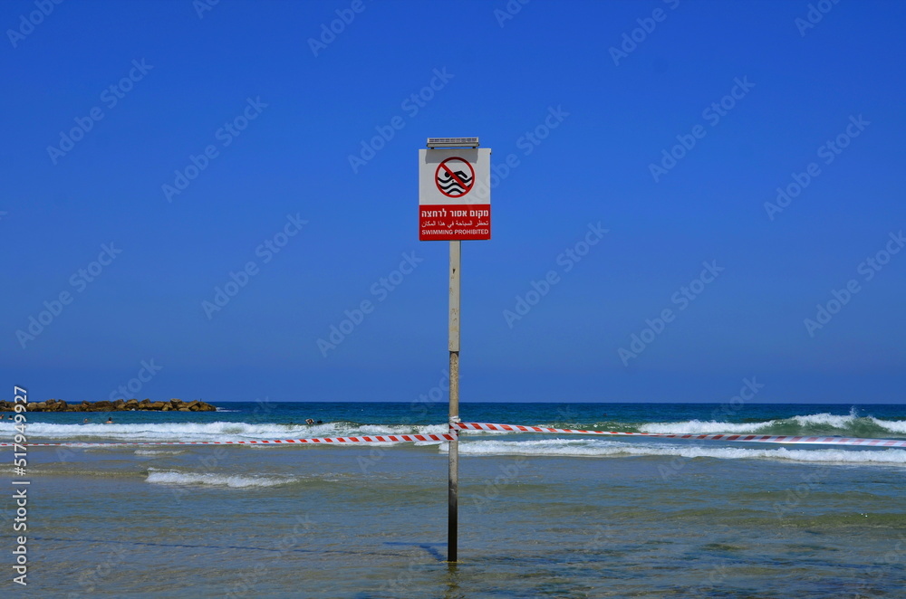 Multilingual warning sign, on the beach in front of an empty sea. A ...