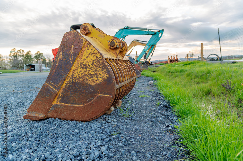 Old rusty excavator bucket close-up. Many excavators in the parking lot ...