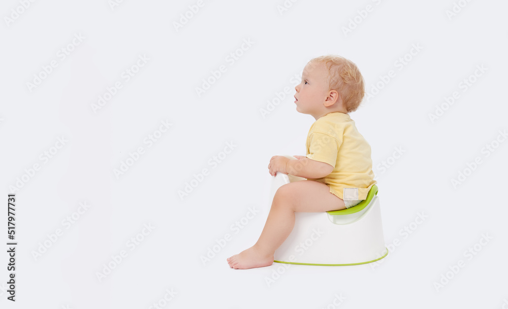 Potty training a baby. Little boy sitting on a potty next to a roll of ...