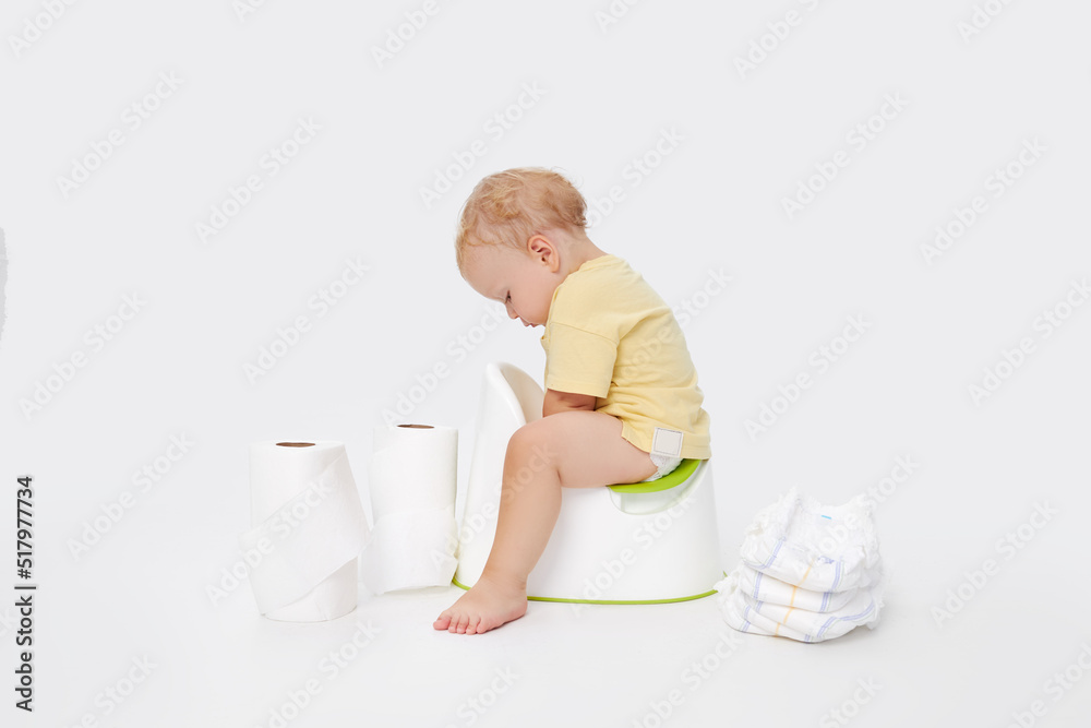 Potty training a baby. Little boy sitting on a potty next to a roll of ...