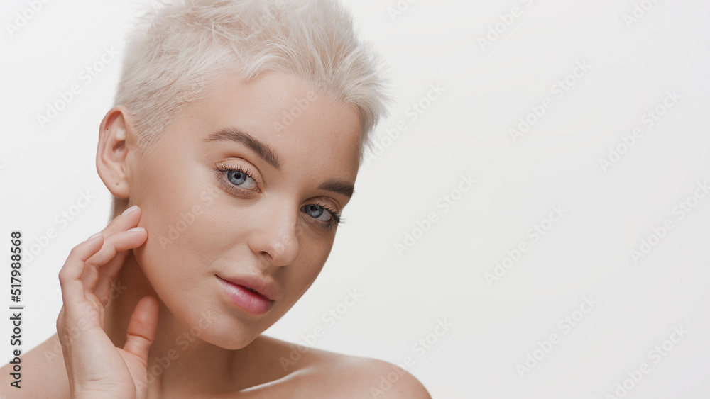 Pretty young slim Caucasian woman with short fair hair strokes her face ...