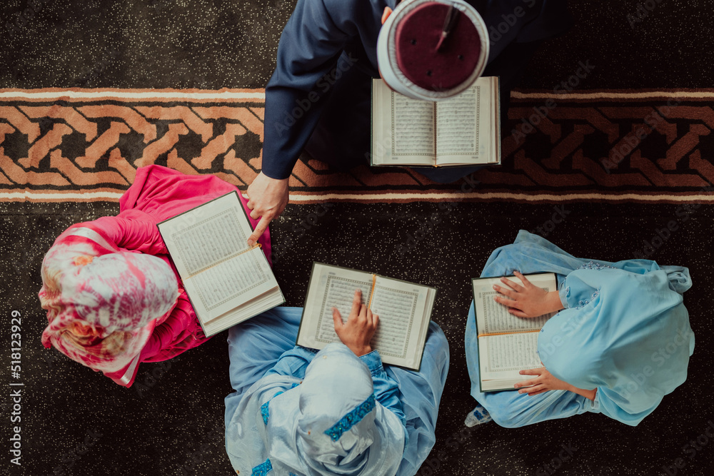 A Muslim teacher teaches a group of children girls to read a holy book ...