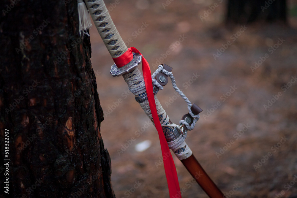 Japanese samurai sword katana with a red ribbon, stands near a tree, on ...