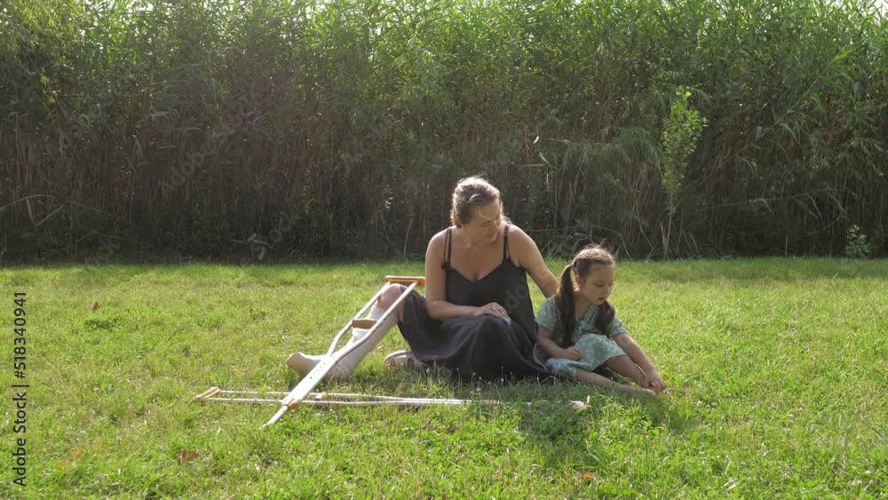 A young girl with a cast and a walker is sitting on the lawn in the ...