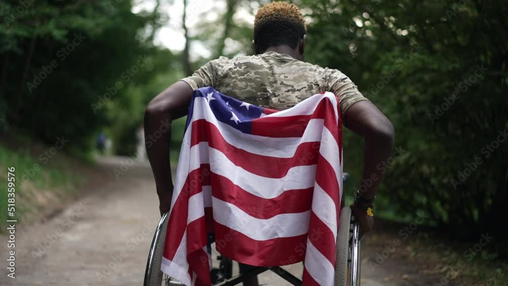 Tracking shot African American young man in wheelchair with US flag ...