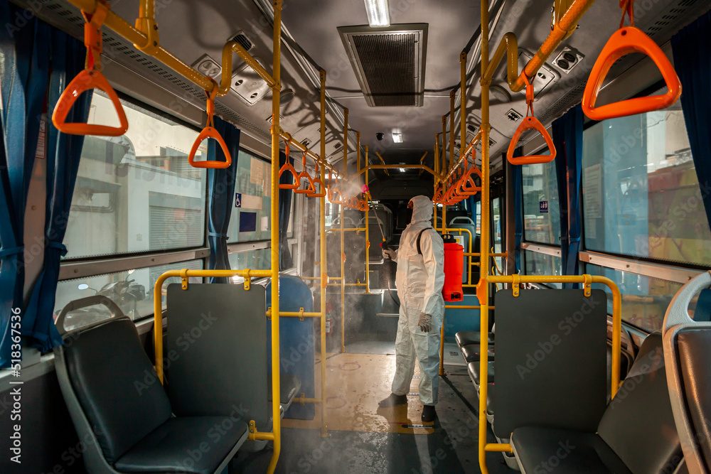 A driver wearing PPE kit in full hazmat suits disinfecting at bus stop ...