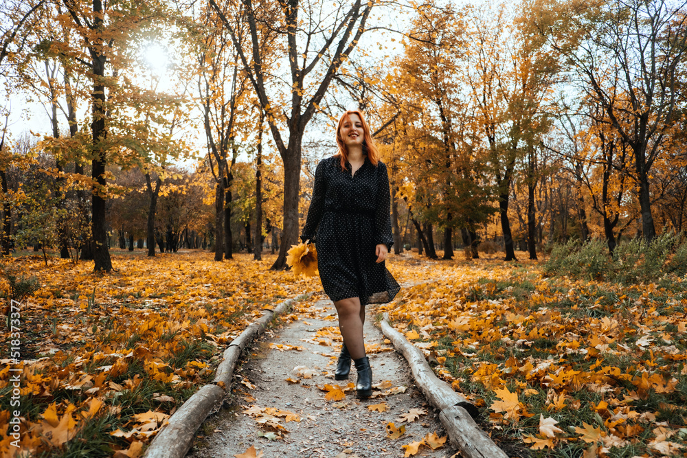 Outdoor autumn portrait of happy smiling plus size red hair woman in dress walking in fall park ...