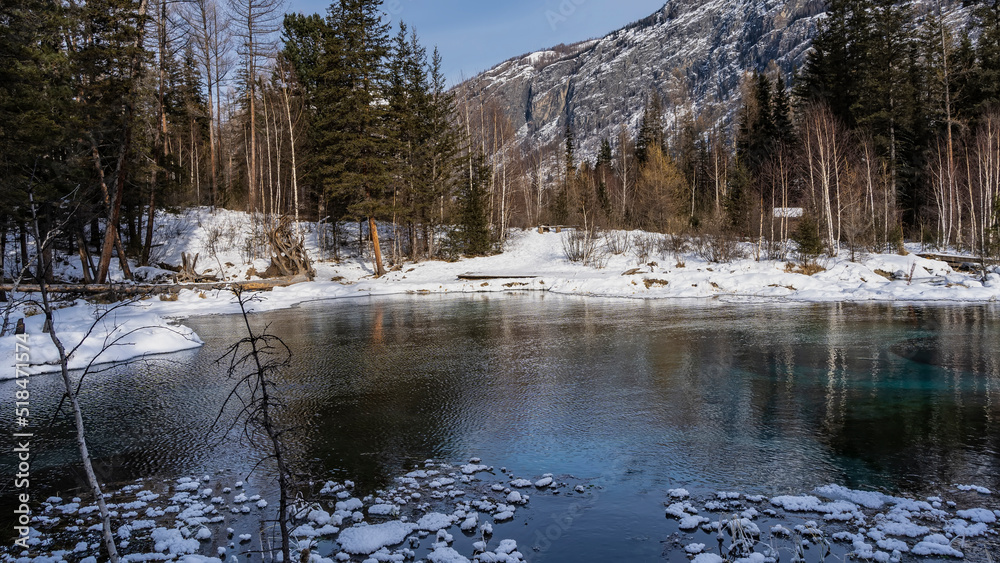 An amazing ice-free lake in the winter forest. Streaks of blue clay are ...