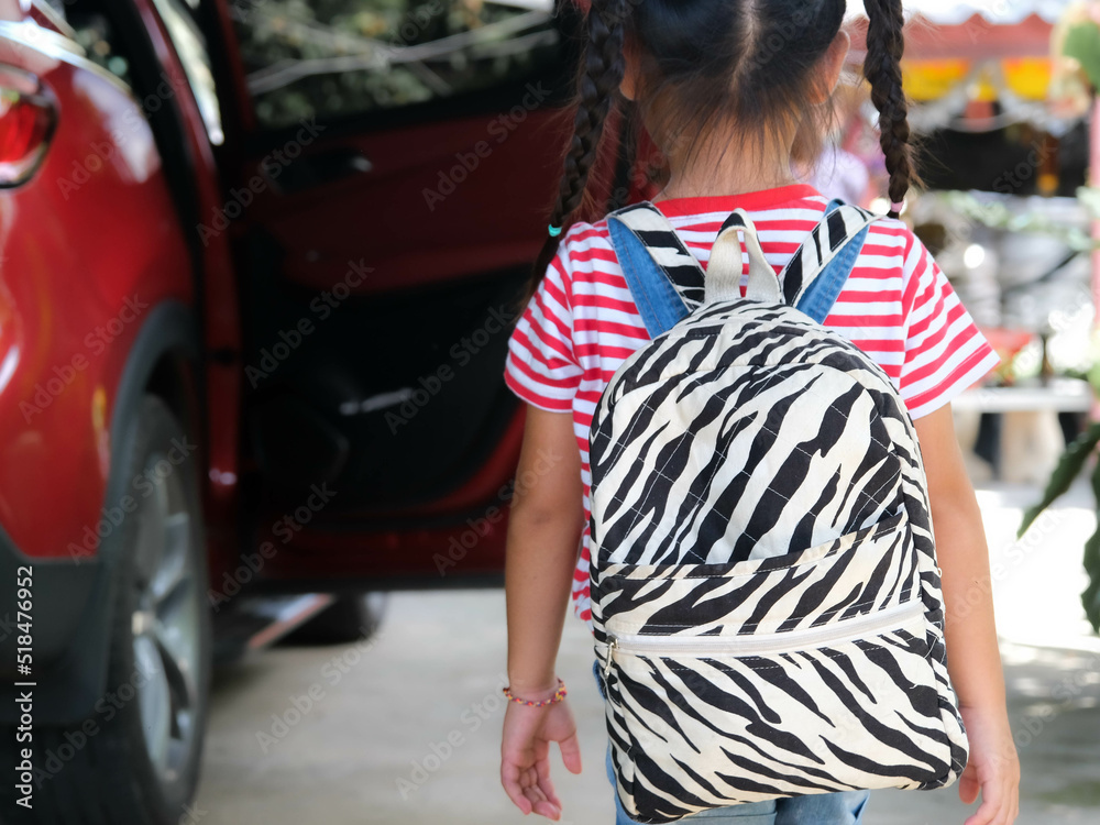 Rear view of happy smiling little girl with backpack getting in the car ...