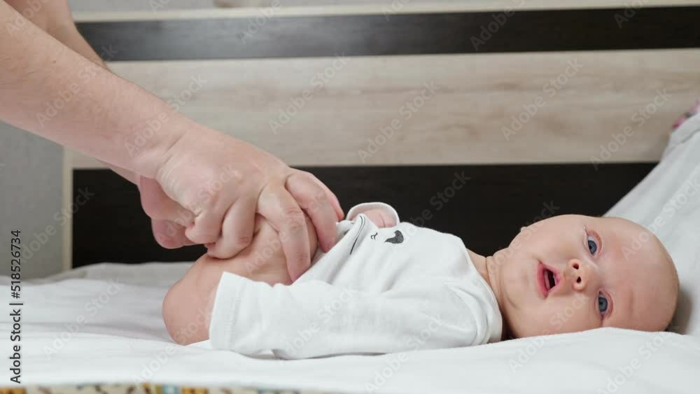 Mother does gymnastics on legs of newborn girl lying on bed. Woman ...