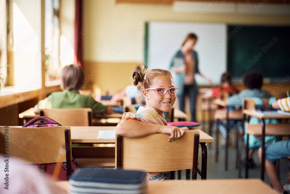 Happy little girl attending class at school and looking at camera ...