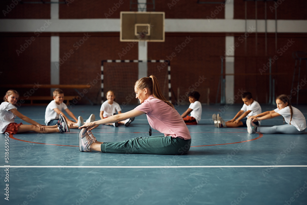 Happy coach and group of elementary students doing stretching exercises ...