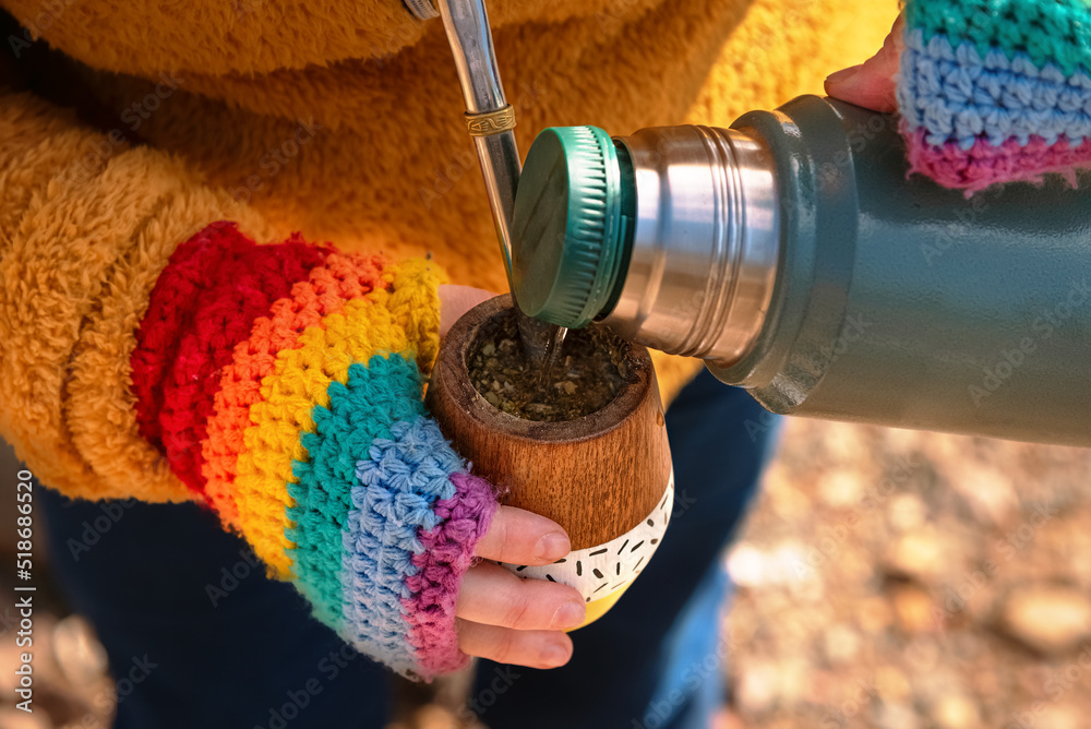 CEBANDO UN MATE CON LAS MANOS ENGUANTADAS. Stock Photo | Adobe Stock