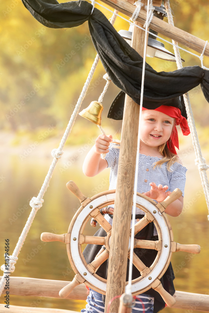 Child in a pirate costume plays on a wooden raft at sunset. Girl ...