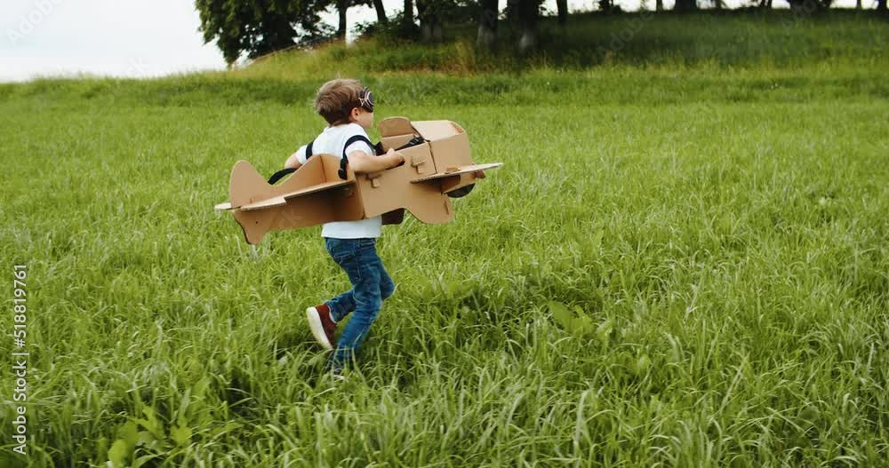 Happy child playing outside on green grass. Kid pilot with a toy paper ...