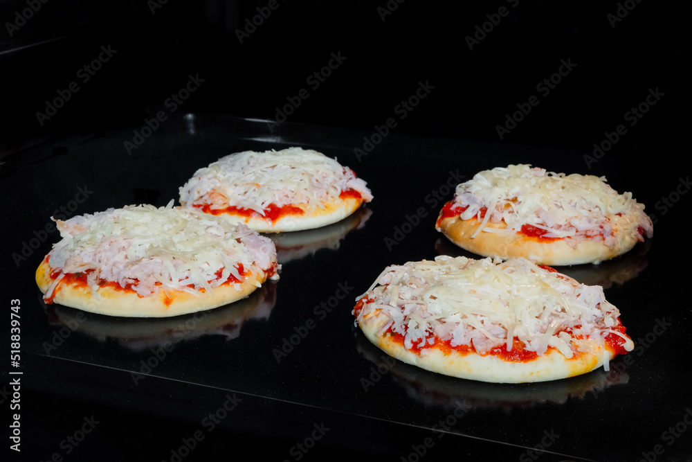 Four mini pizzas with ham, cheese and sause baking on tray in electric ...