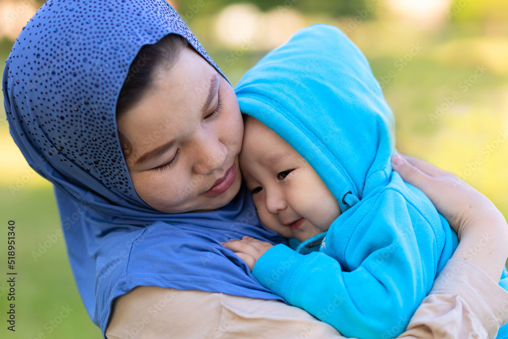 Cute young islamic kazakh woman hugging her little crying son, newborn ...