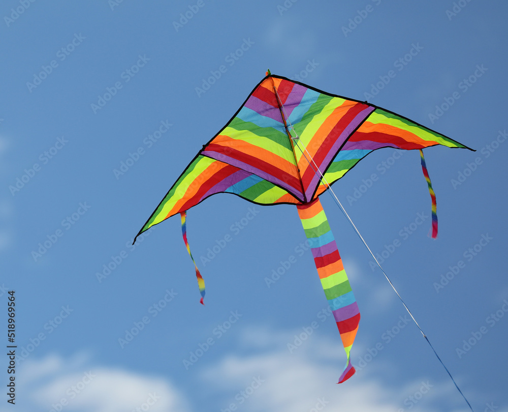 colorful triangular kite that flies high in the sky with some clouds ...