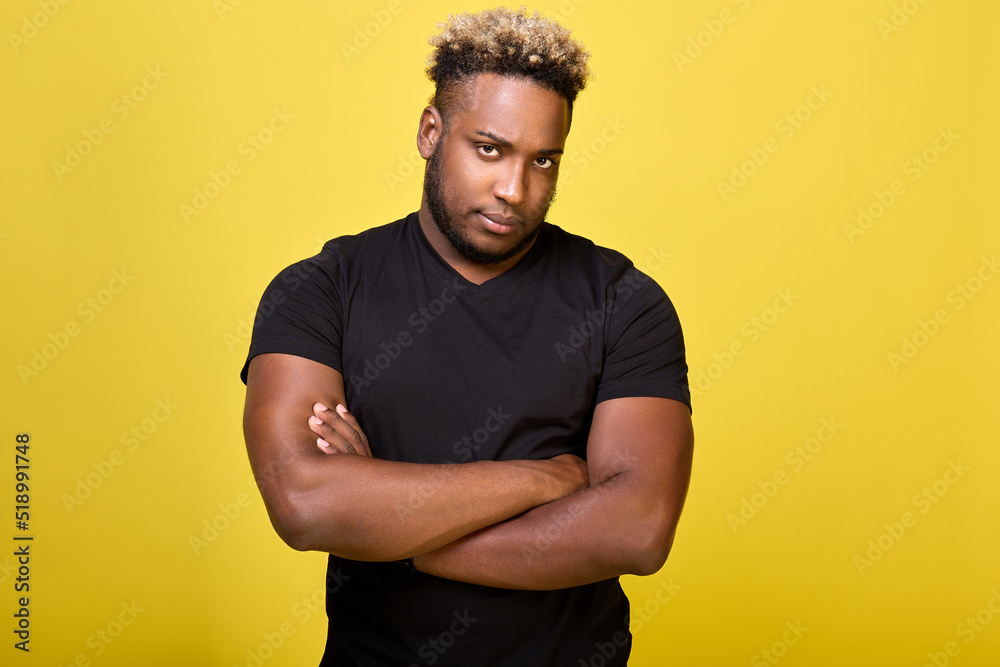 Strong guy with big muscles stands in a T-shirt on a yellow background ...