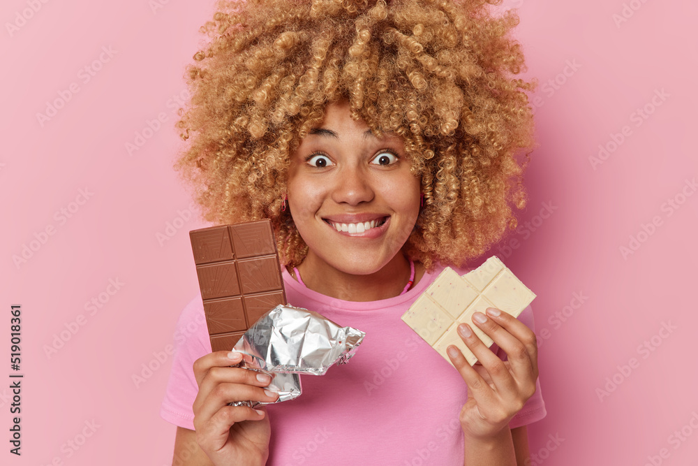 Positive curly haired woman holds two bars of sweet chocolate has sugar ...