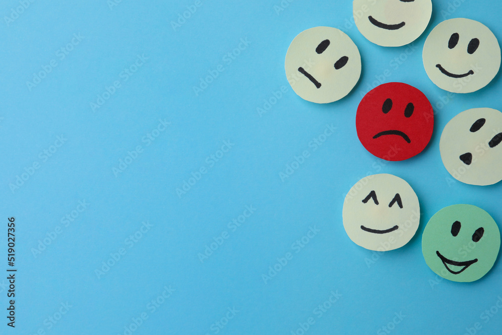 Many faces with different emotions on light blue background, flat lay ...