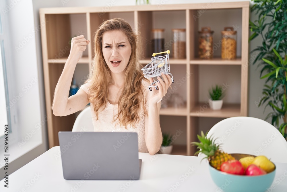 Beautiful blonde woman shopping online with laptop annoyed and ...