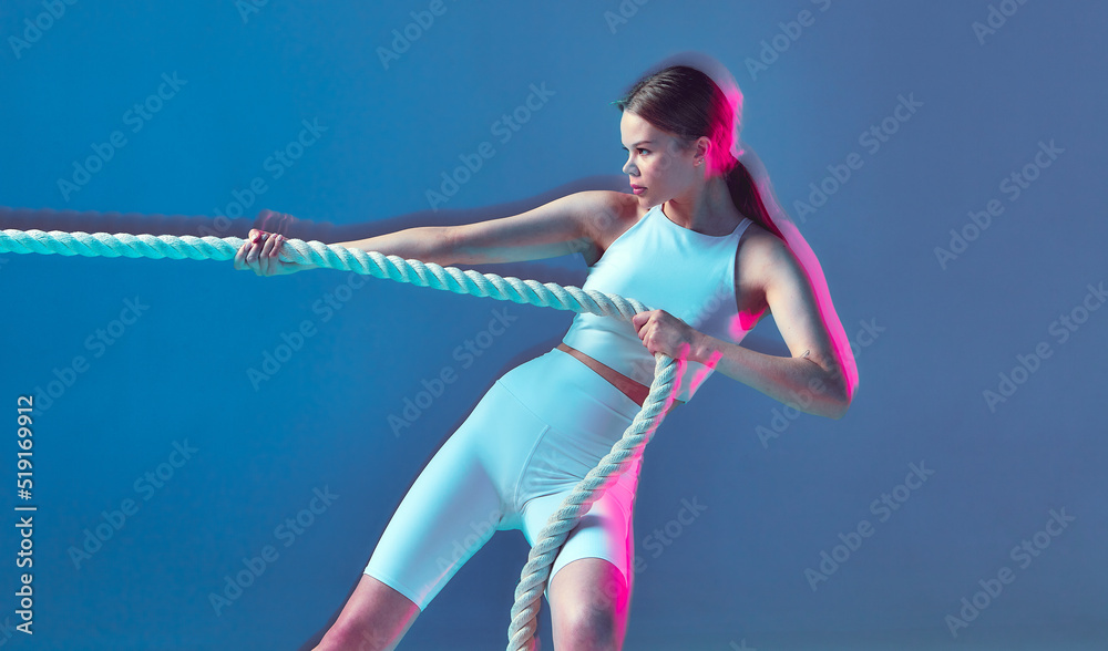 Strong athletic girl pulling sports rope during endurance workout in ...