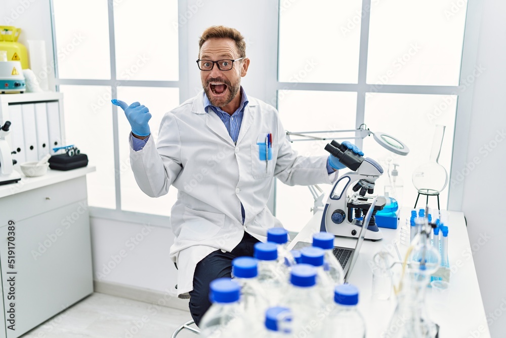 Middle age man working at scientist laboratory pointing thumb up to the ...
