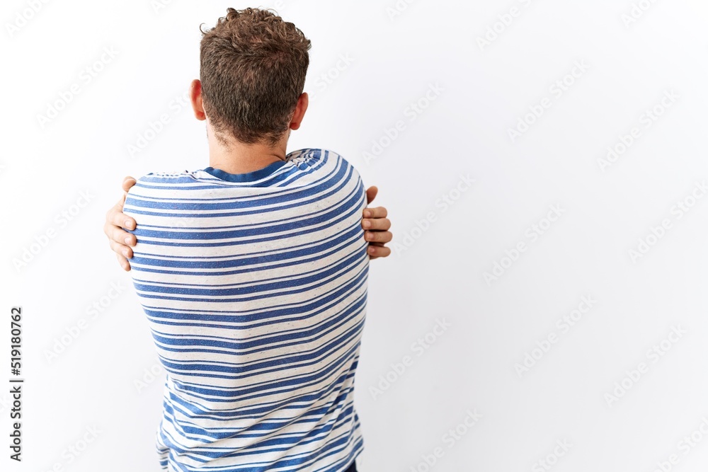 Handsome young man standing over isolated background hugging oneself ...