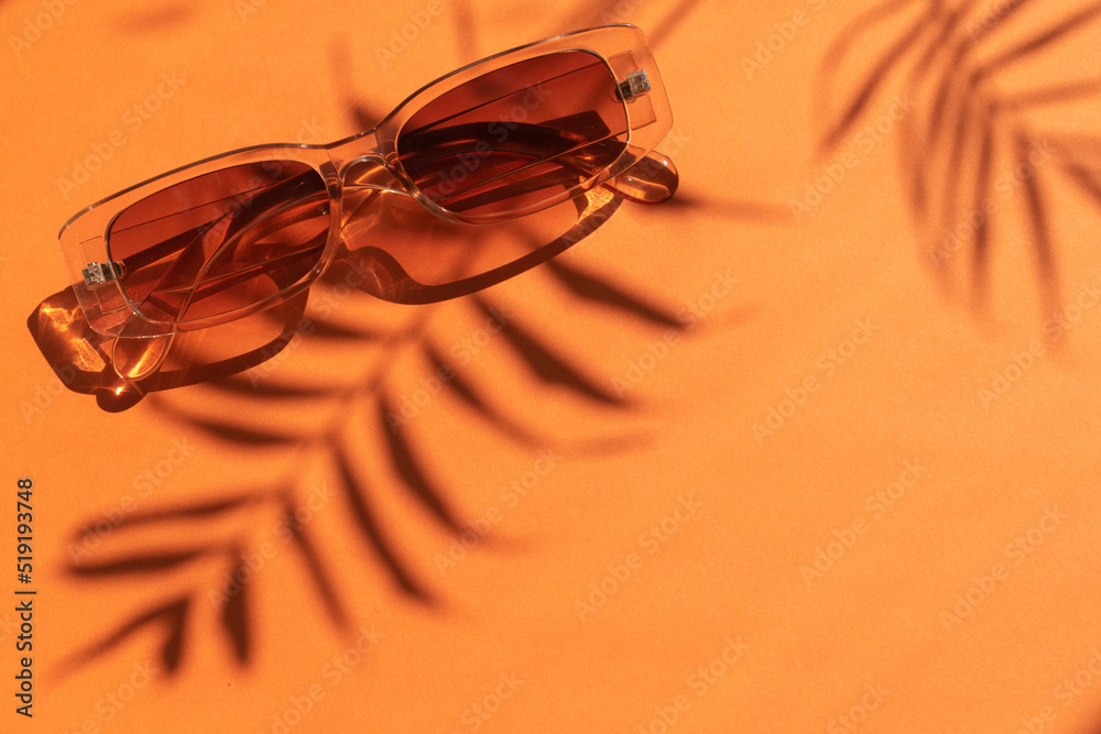 Orange sunglasses on an orange background with shadow from a palm tree ...