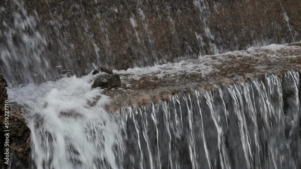 The flow of water from the dam of a mountain lake through a metal mesh ...