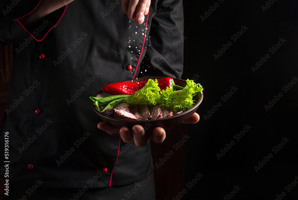 Chief sprinkles salt on a sliced steak with beef and vegetables in a ...
