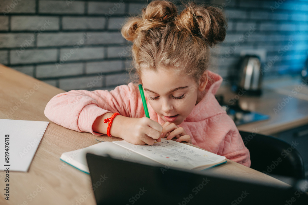 Schoolgirl sitting at desk doing her homework using a tablet computer ...