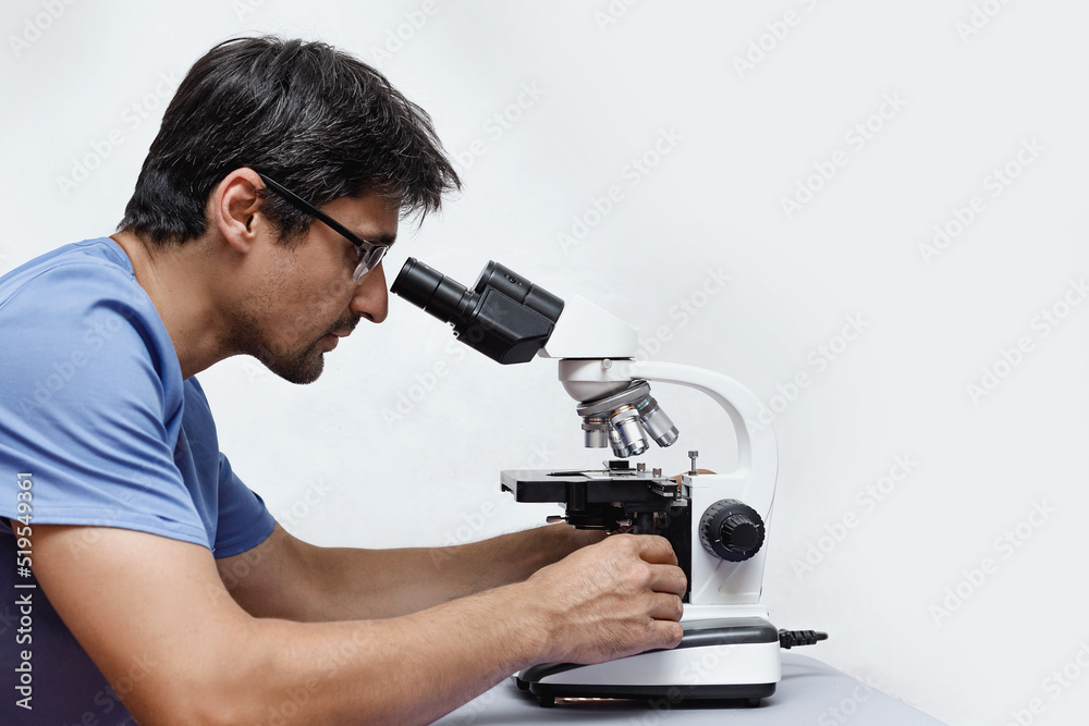 A brunette histologist doctor in a blue medical uniform looks in a ...