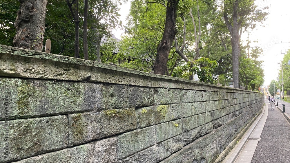 old rustic stone wall along the straight road beside ancient Japanese ...