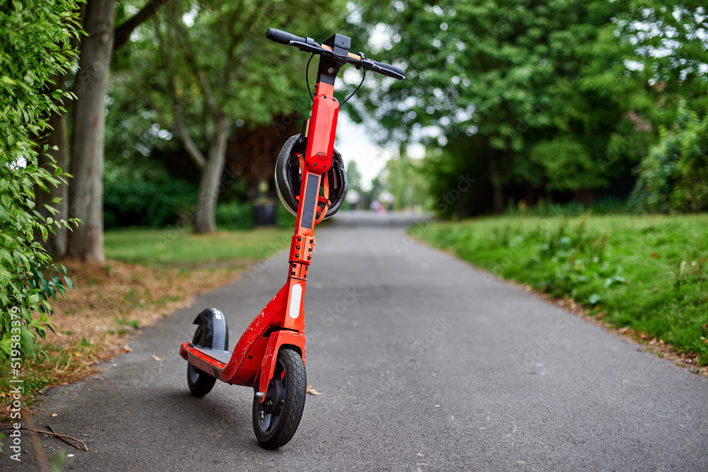 An orange electric scooter stands in the park against the background of ...