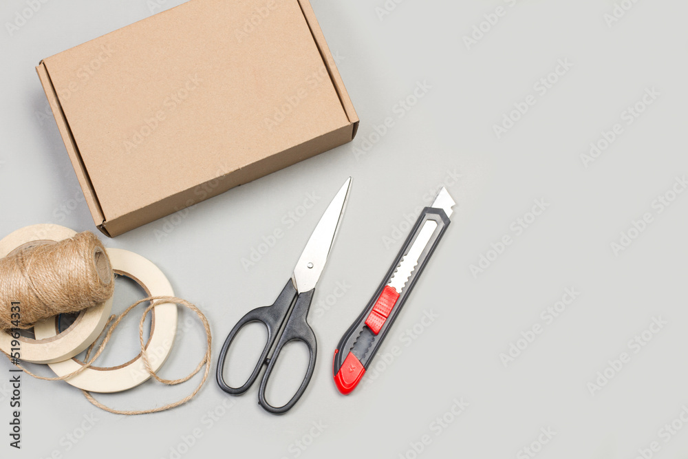 Caja de cartón marrón junto a una tijera, un cuter, cinta adhesiva e ...