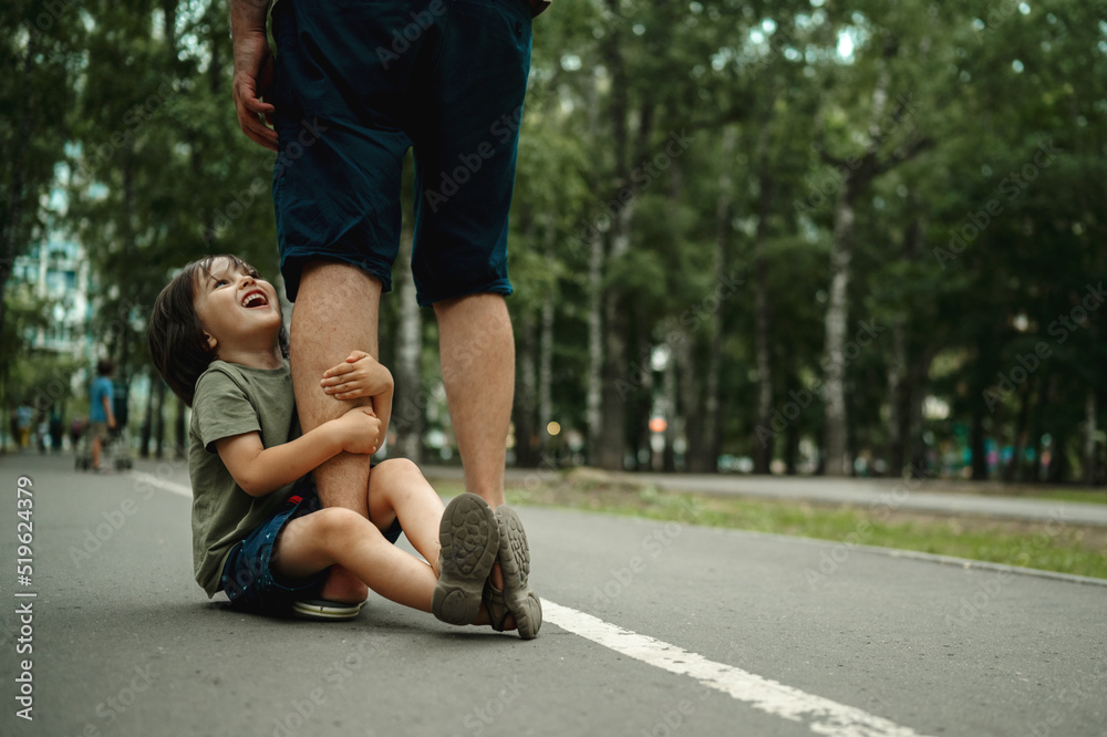 Dad and son are walking in the park, the child is hanging on his father ...