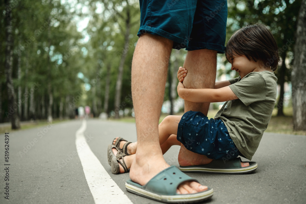 Dad and son are walking in the park, the child is hanging on his father ...