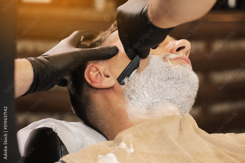 Barber Man is shaving client with a vintage straight razor in a ...