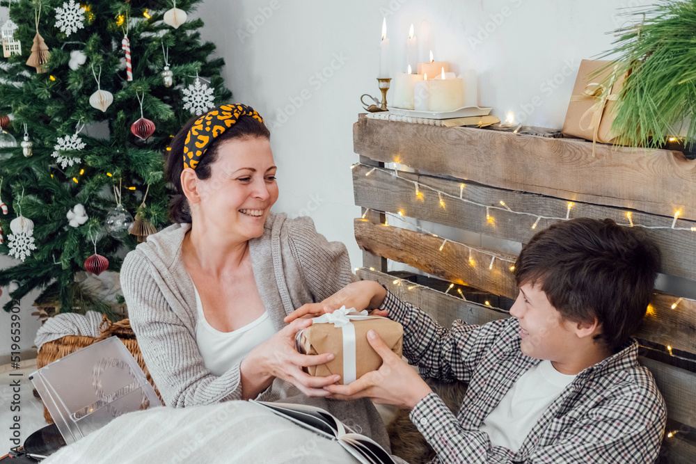 Boy receiving a Christmas gift from her mother. Smiling parent giving ...