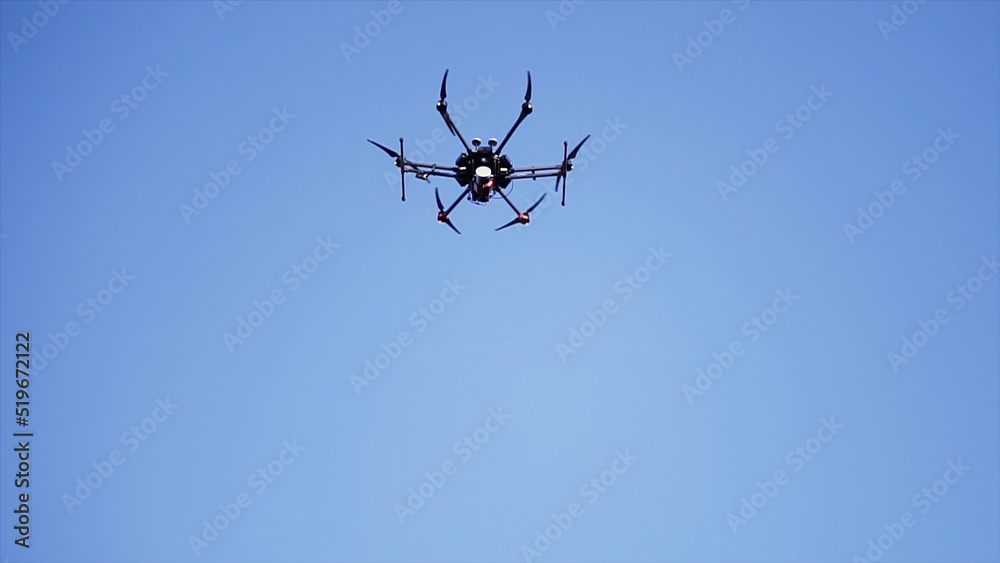 Black drone flying against the blue sky with spinning blades, bottom ...