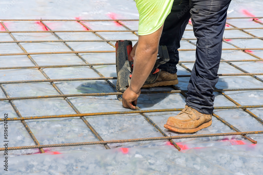 For cement foundation, construction worker twists steel bars with wire ...