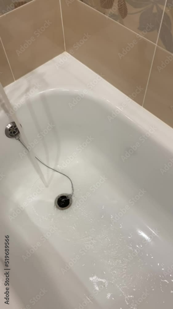 Female's hand opens the water tap and draws water into the tub. Rubber ...