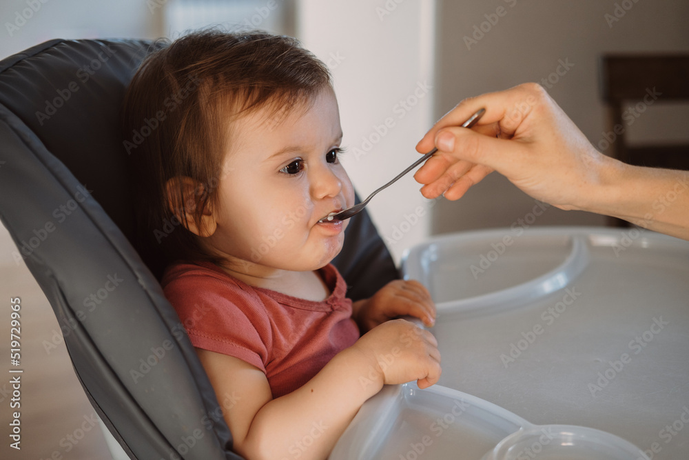 Mother hand giving food with spoon to her eight-month child at home ...