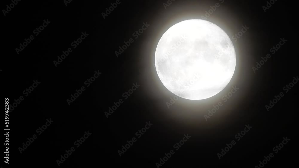 Glowing huge full moon as seen from earth through the clouds against ...