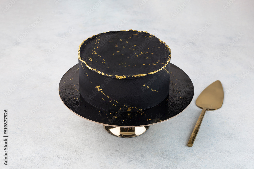 Chocolate cake with black icing, decorated with gold sequins on a white ...